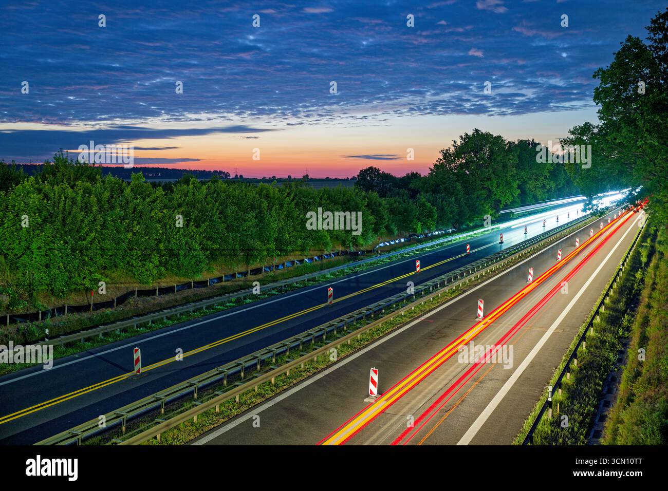Evening autobahn divided by a barrier, trees line the sides, one lane ...