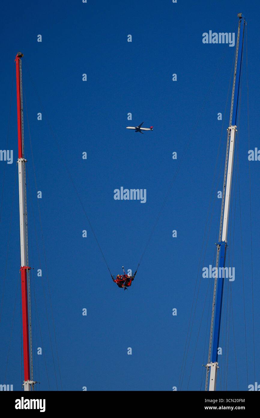 An airplane flies overhead as two fair attendees ride the Sling Shot ...