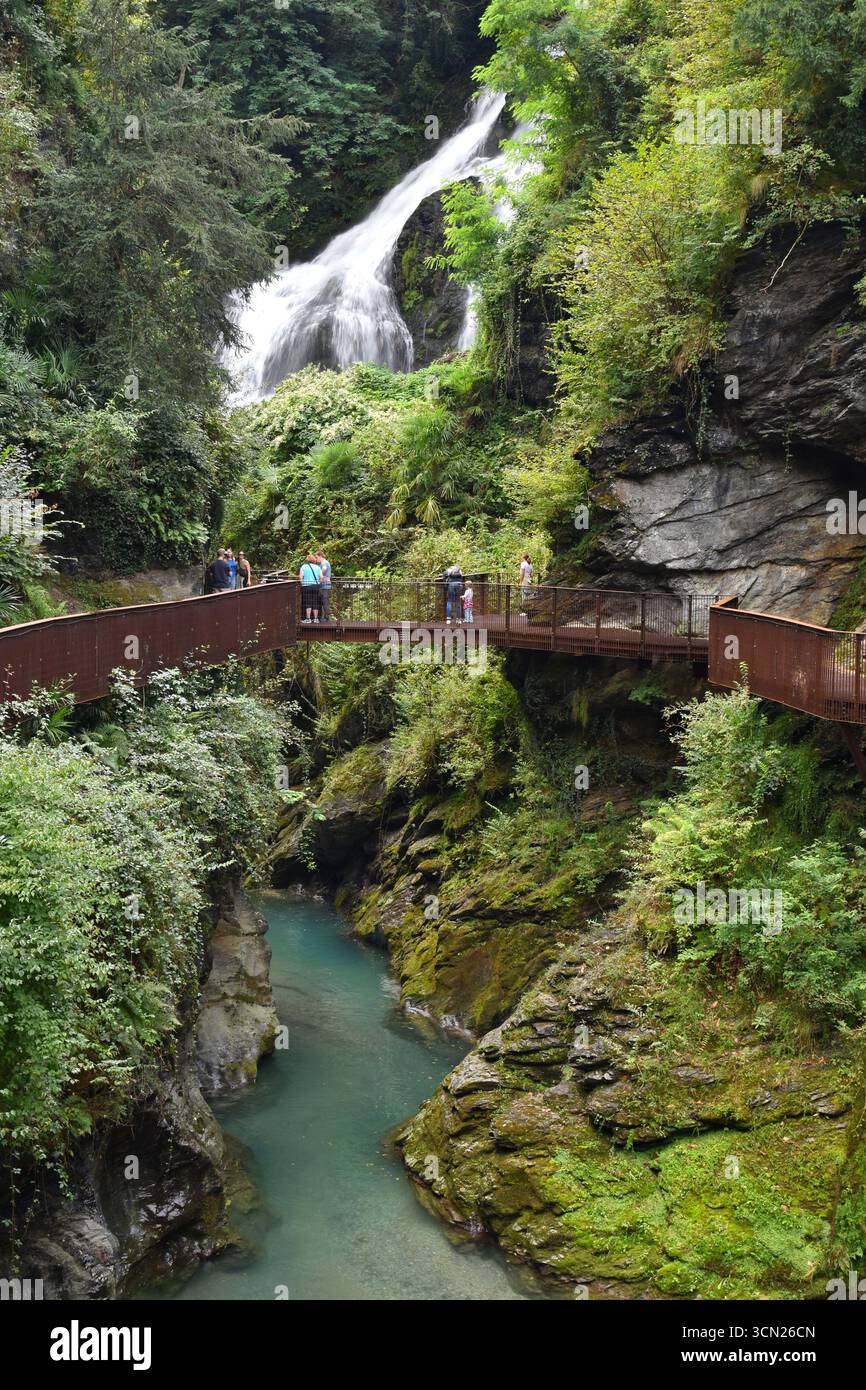 Lush green vegetation, a tumbling waterfall into a gorge, and a walkway ...