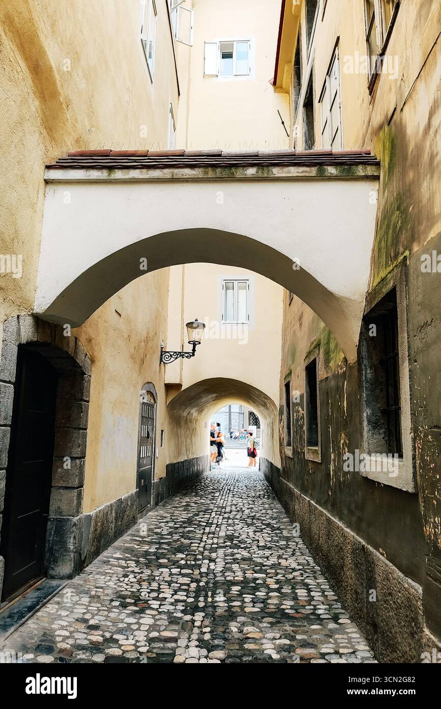 Narrow cobblestone alley with arch and historic buildings in an old ...