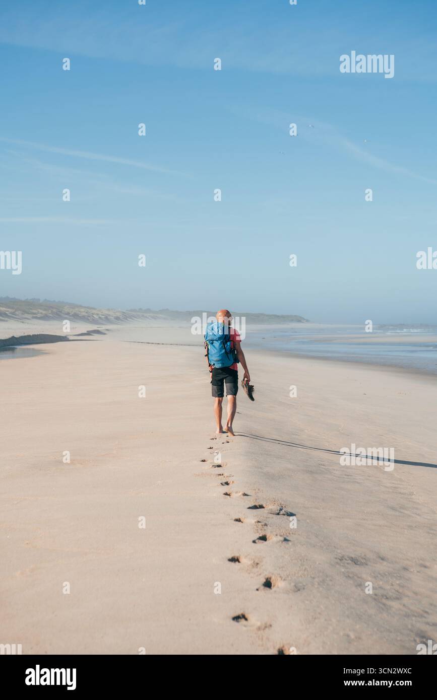 Lonely barefoot backpacker man walking by sandy Portugese beach in ...