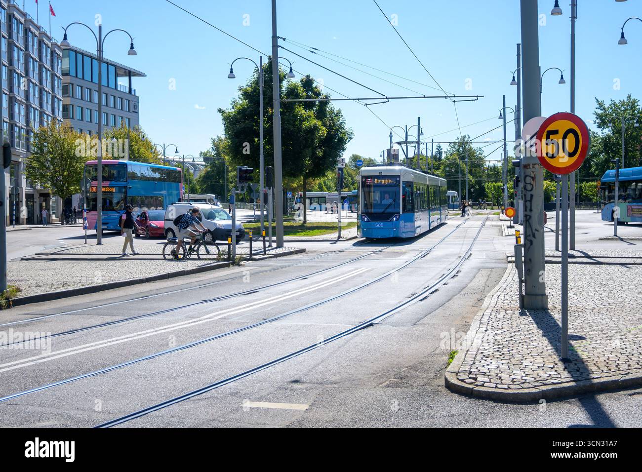 People walk and ride bikes near a tram stop on a clear day. Trams wait ...