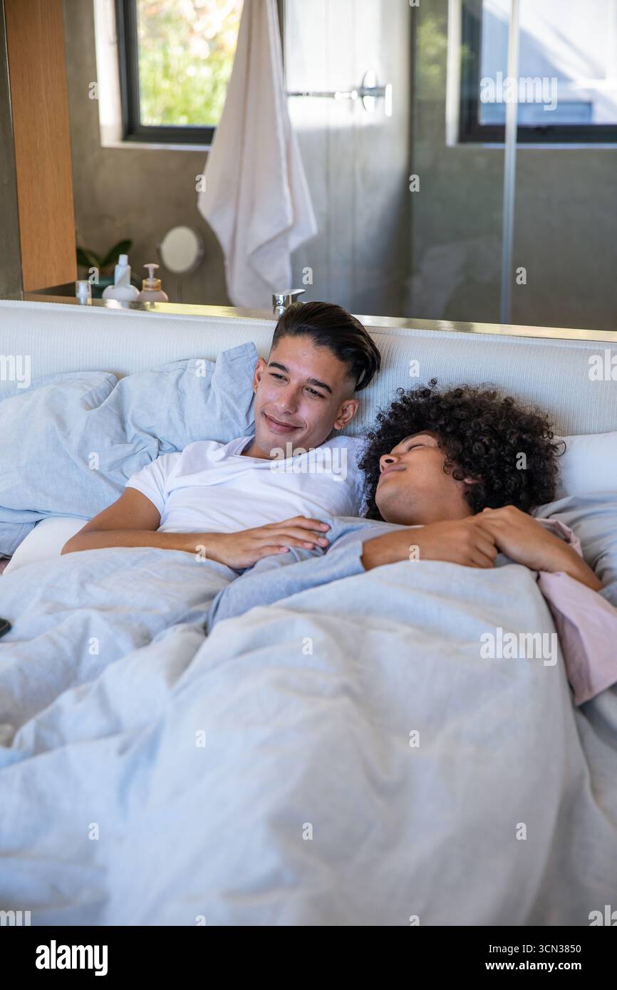 Diverse male partners lying under light gray duvet against white ...