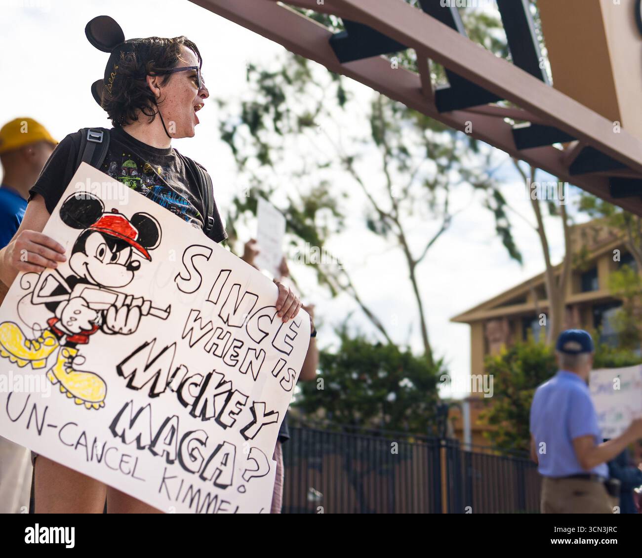 A protester wearing Mickey Mouse ears holds a placard reading “Since ...