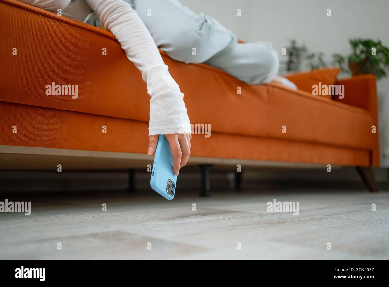 Young woman napping comfortably on an orange sofa at home, hand nearly ...