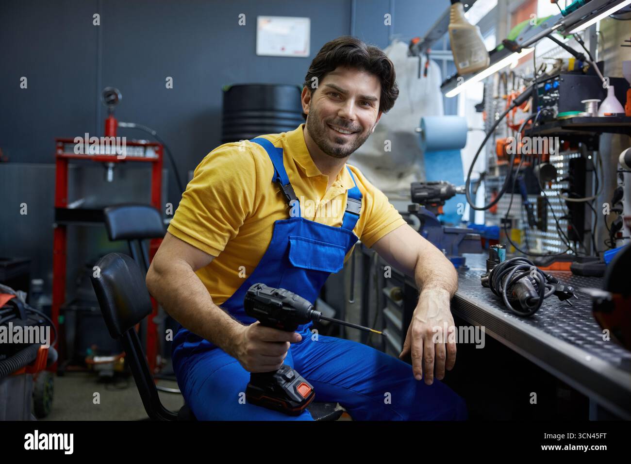 A man worker sits comfortably in a chair, holding a drill and smiling ...