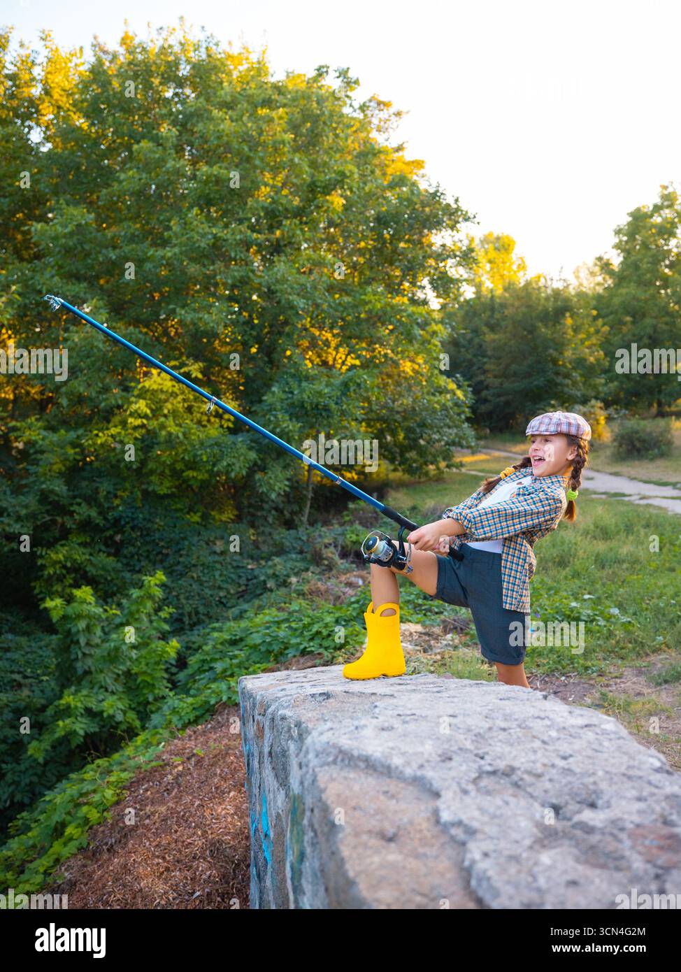 Happy girl in yellow boots fishing with rod on stone bridge Stock Photo ...