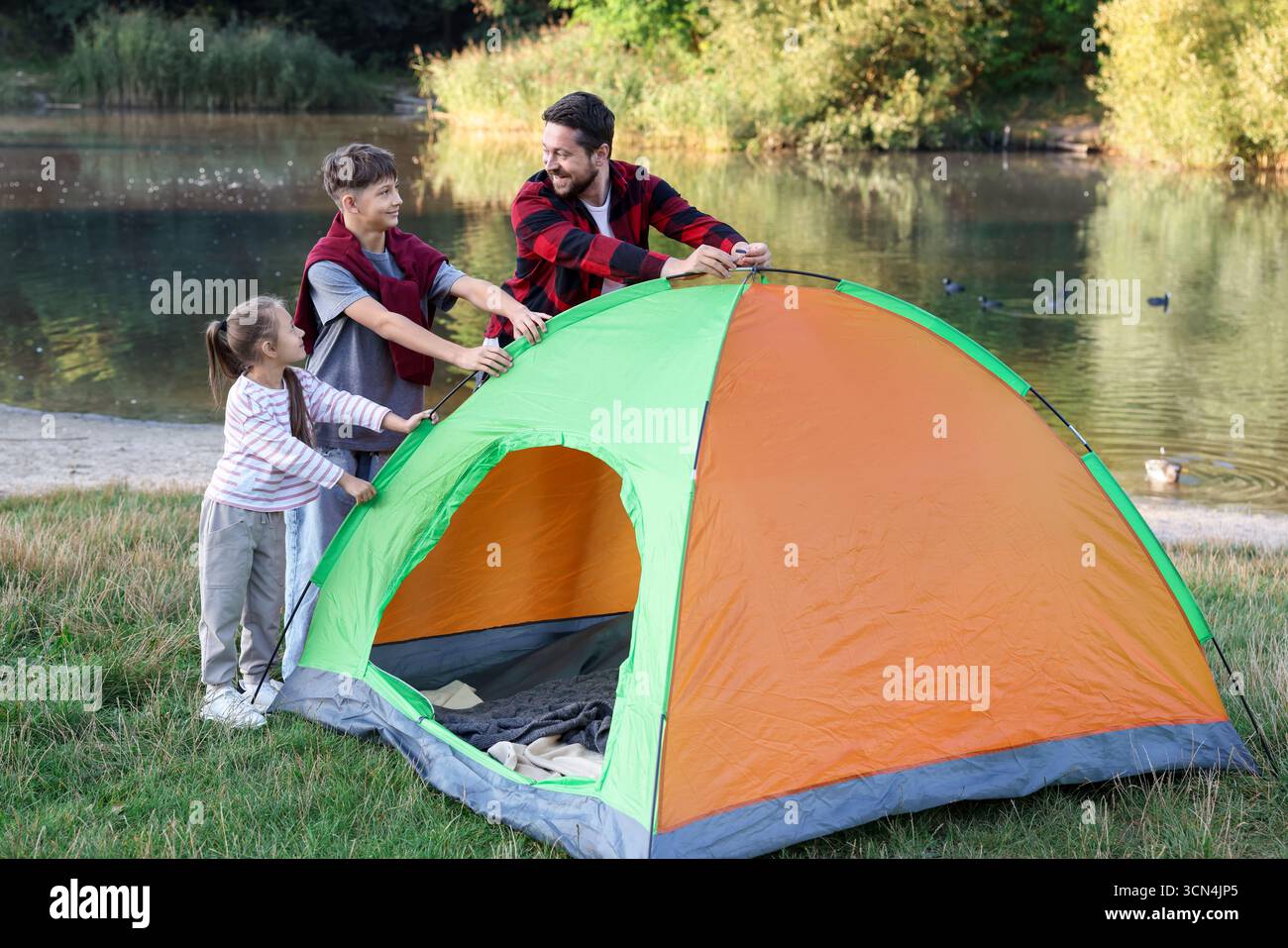Happy father and his children setting up camping tent near river ...