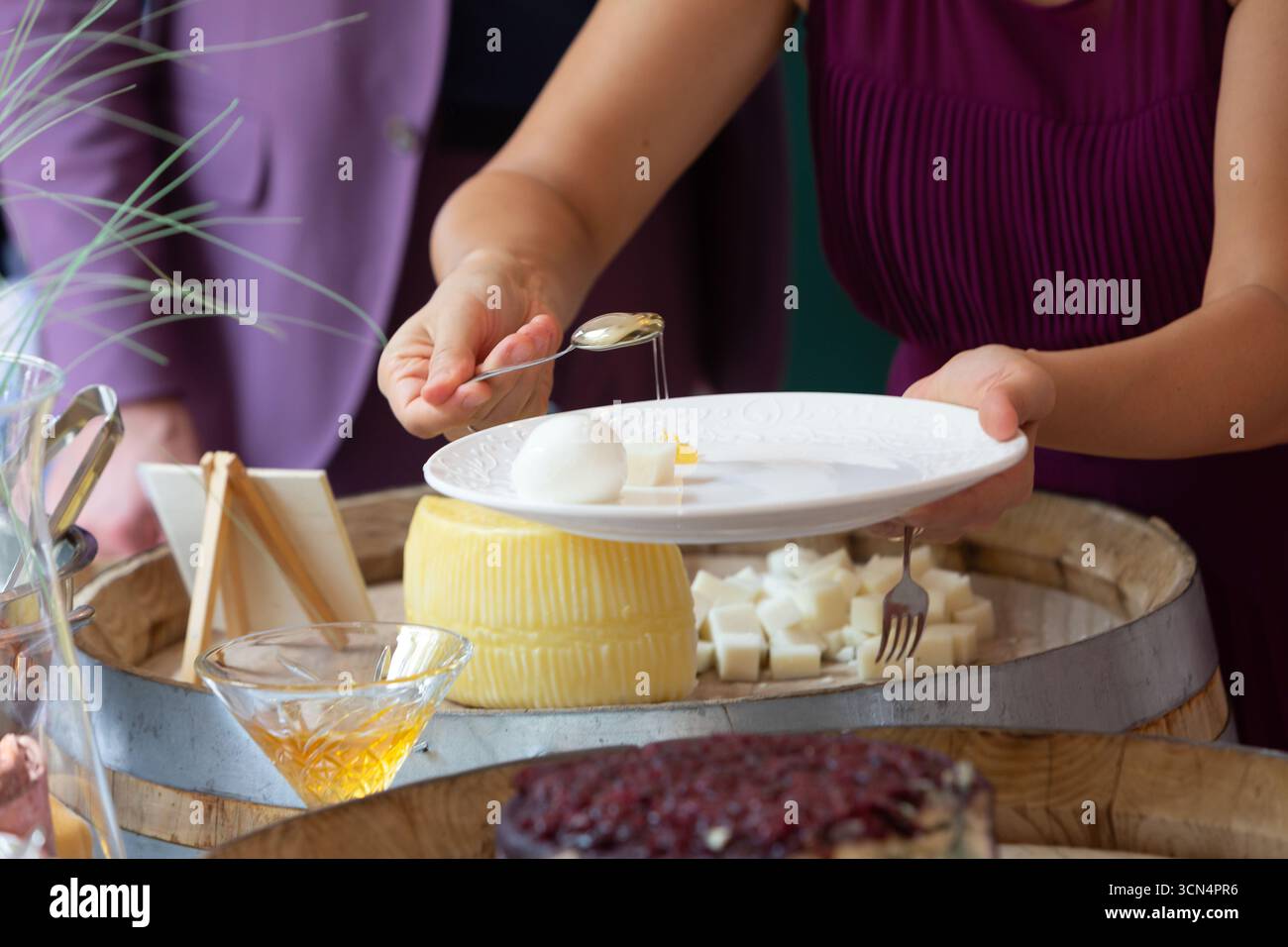Guest pouring honey on a fresh mozzarella ball at a buffet table, ready ...