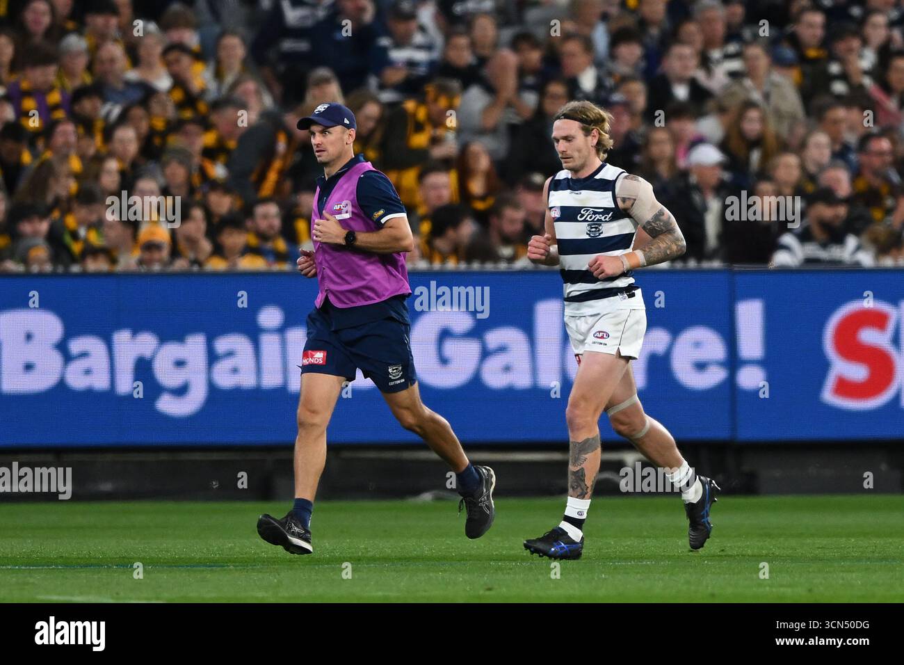 Tom Stewart of Geelong (right) exits the field after sustaining an ...