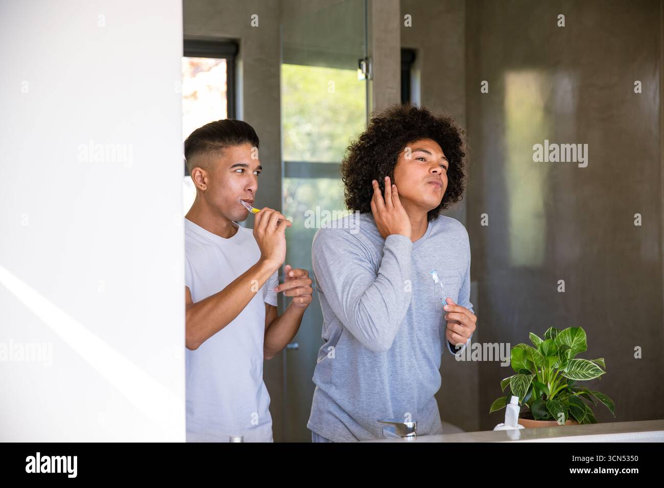 Diverse male friends brushing teeth at bathroom counter with ...