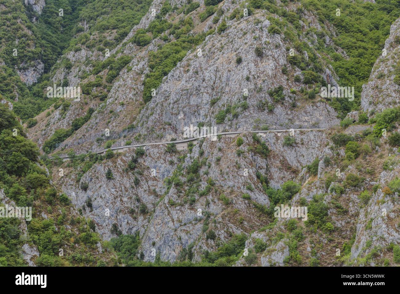 View of rugged, sun-drenched cliffs meet lush greenery, as a thin road ...