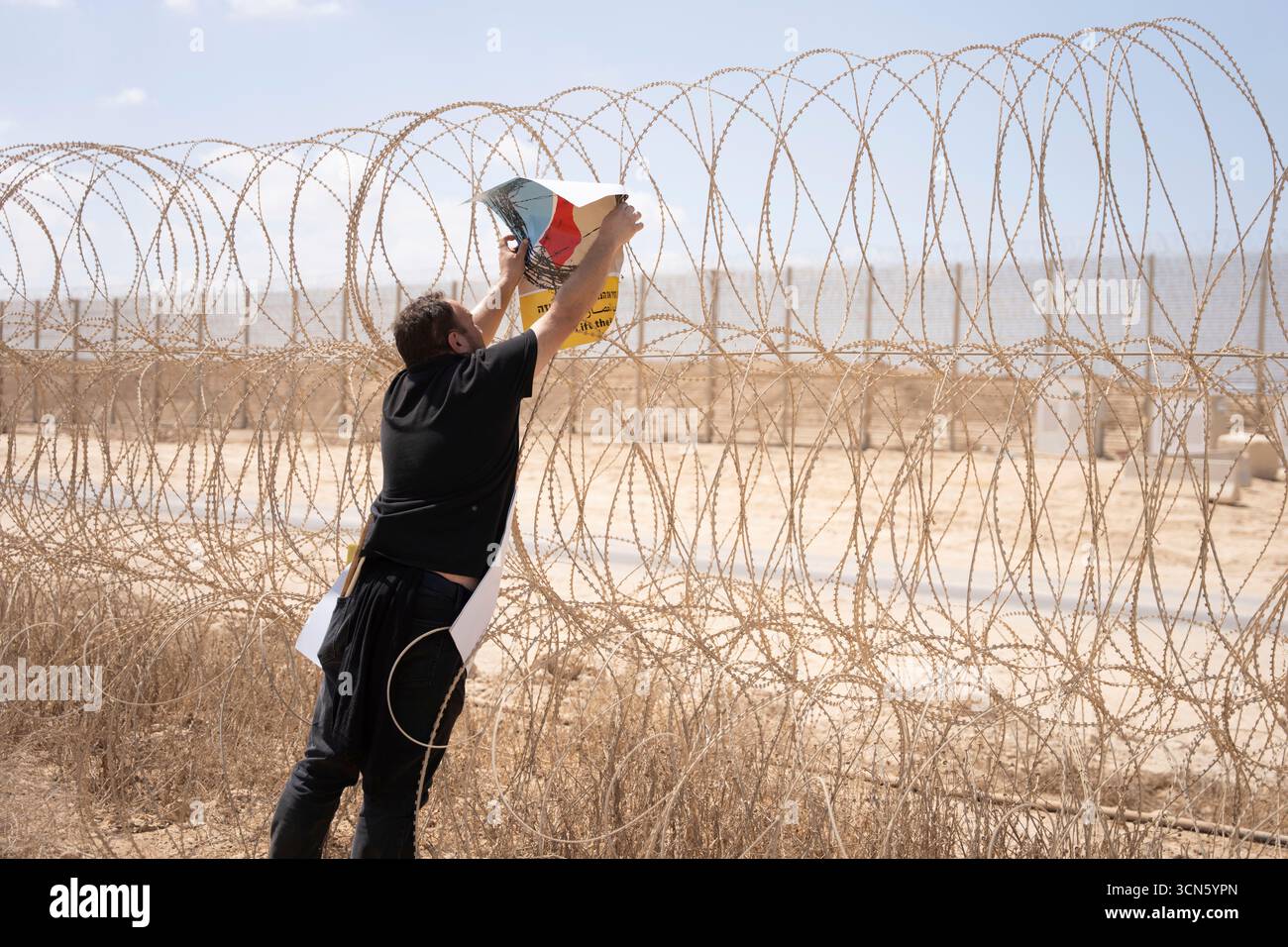 An activist holds up a sign near razor wires during a protest against ...