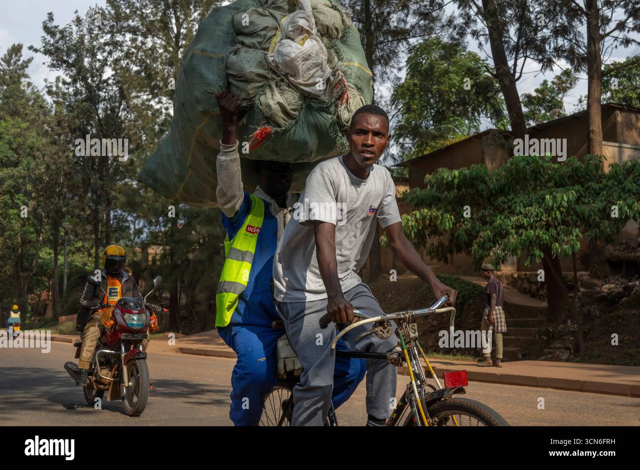 A man carries a heavy load as he rides on a velo-taxi in Kigali, Rwanda ...