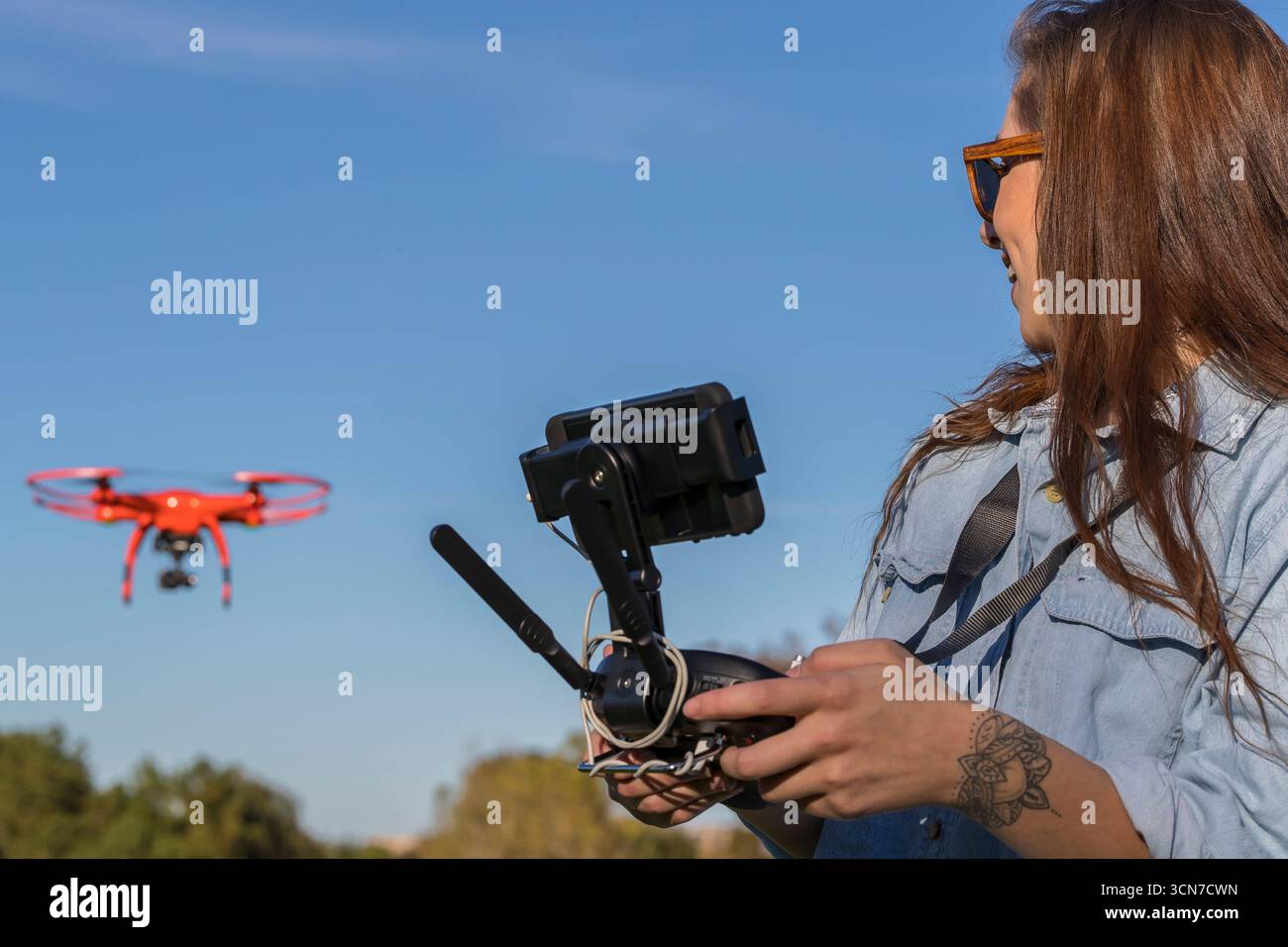 A beautiful young woman skillfully pilots a drone under the bright sun ...