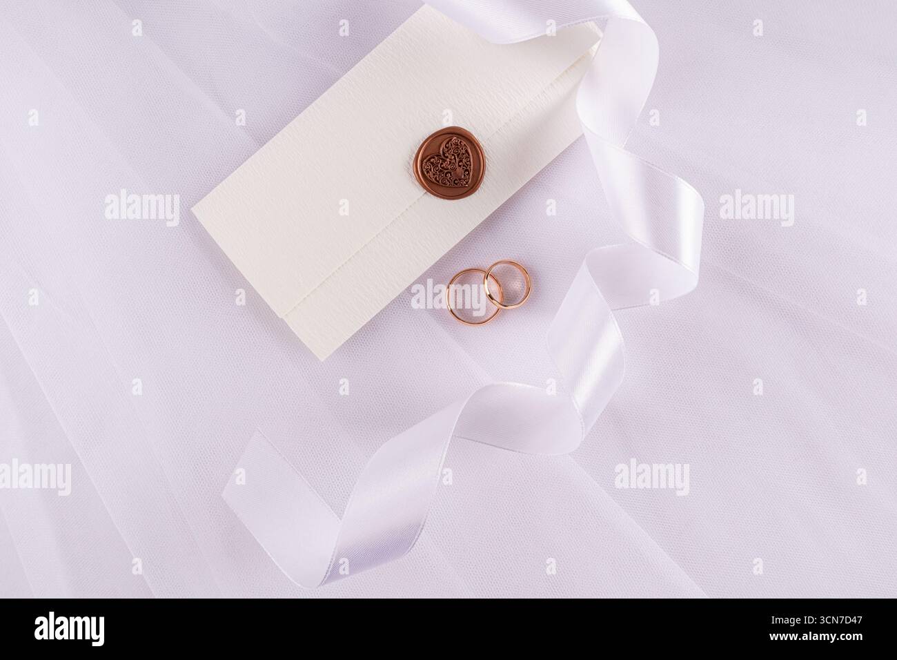 Two gold wedding rings lie on the folds of the bride's white veil with ...