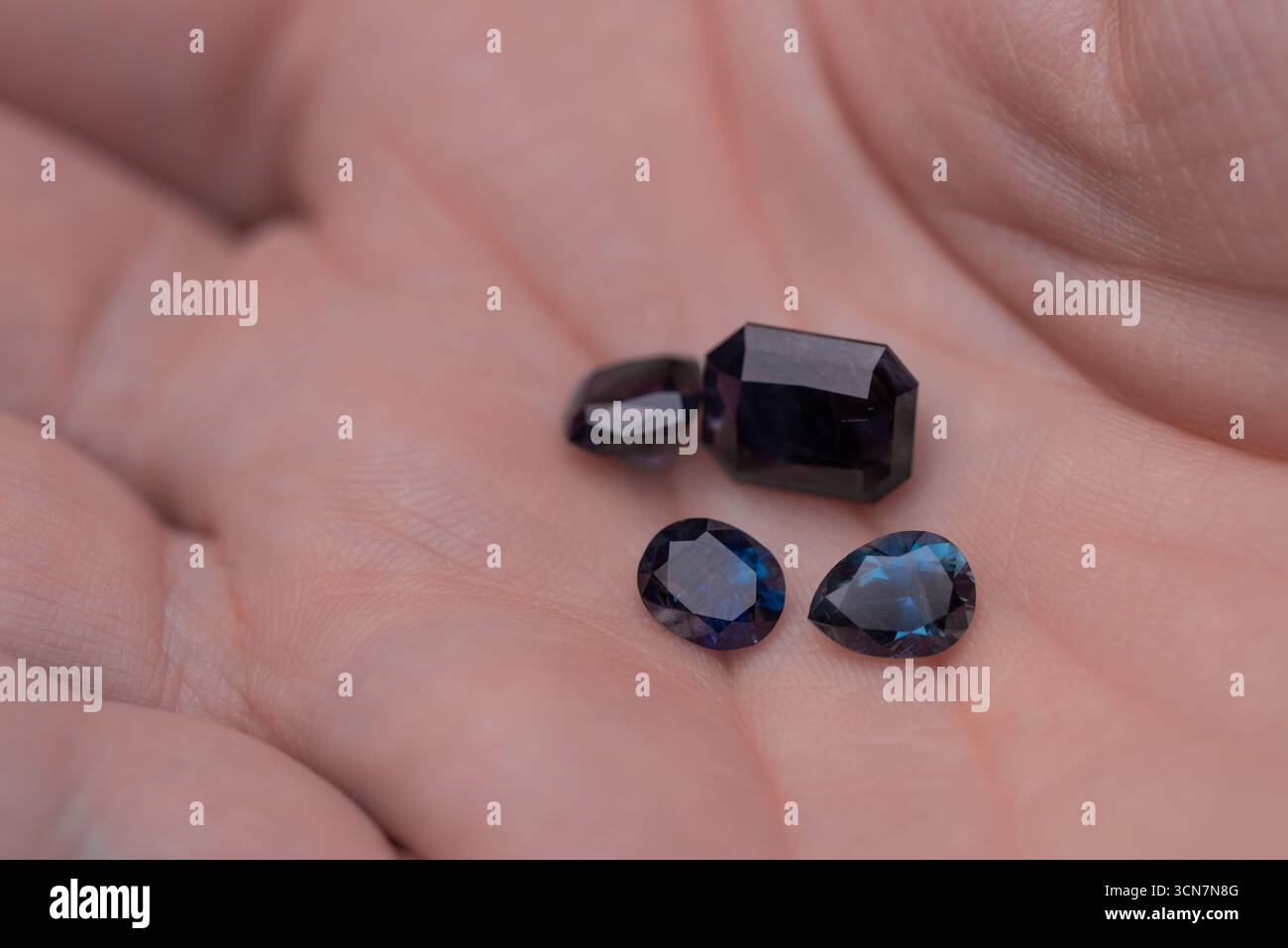 A hand is holding four blue gems, including a blue diamond. The gems ...