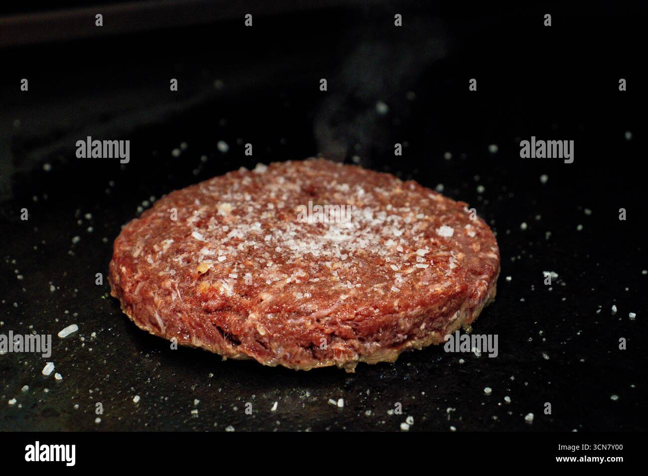 raw beef patty ready for the grill. The rich, red meat is generously ...
