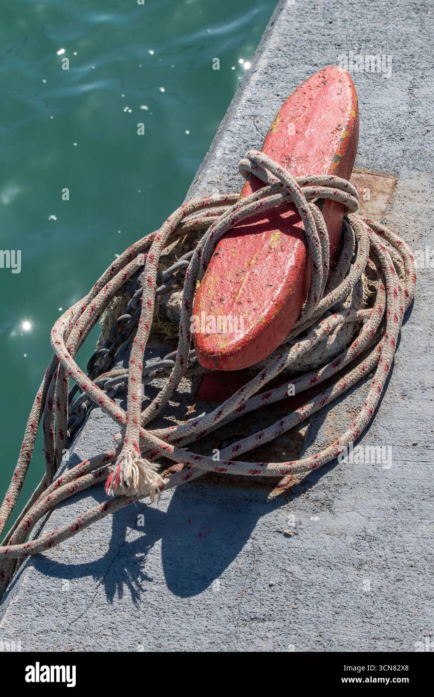red-painted old metal cleat on a dockside with old rope wrapped around ...