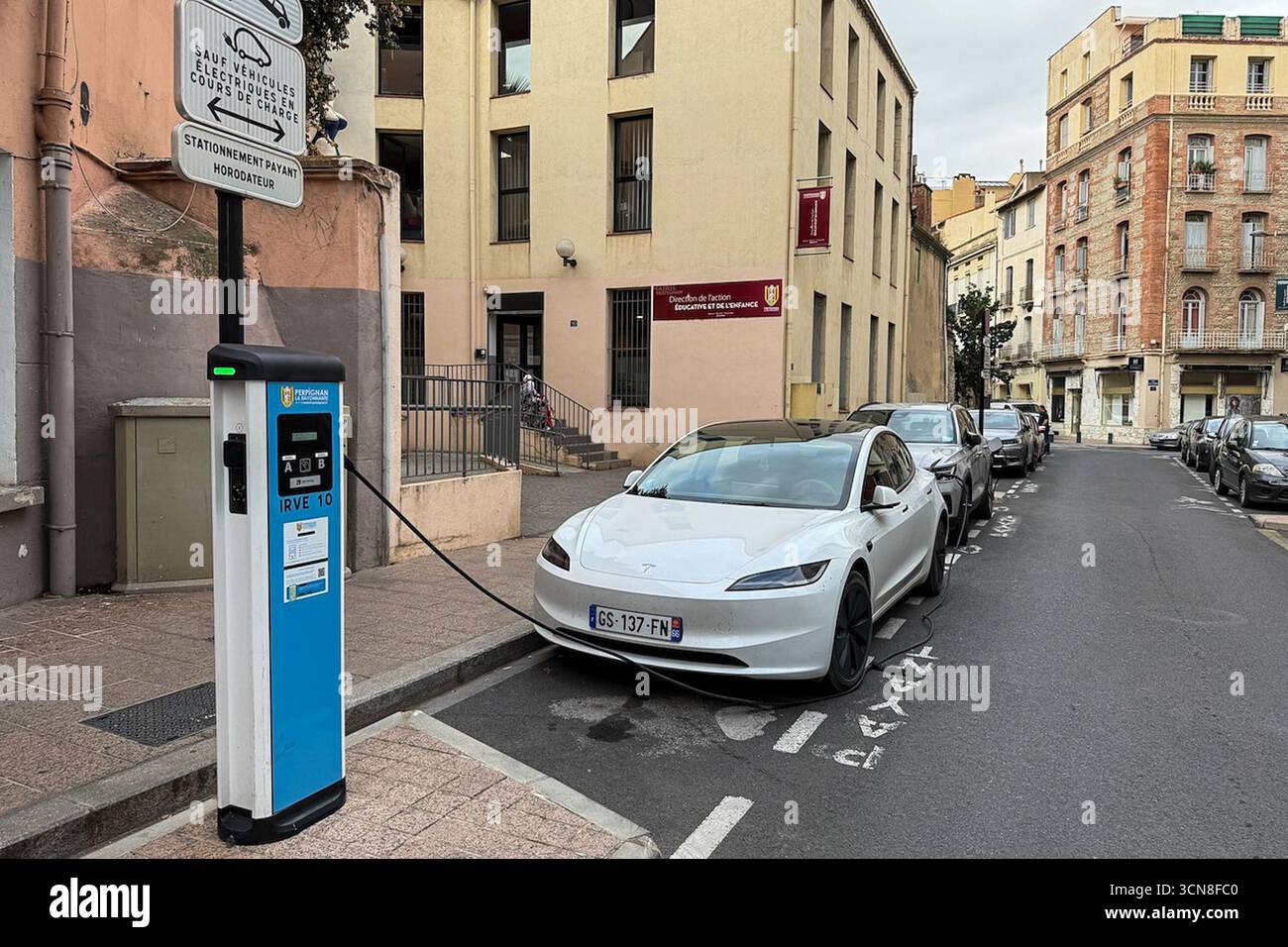 A white Tesla electric vehicle is plugged into a curbside charging ...