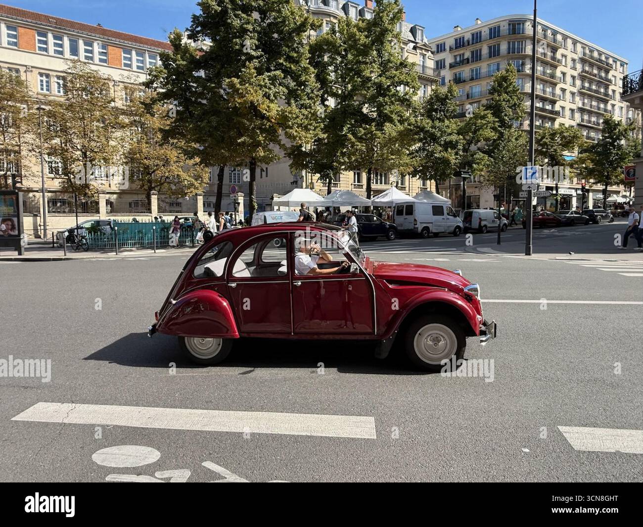 A street scene in Paris featuring a vintage red Citroën 2CV driving ...