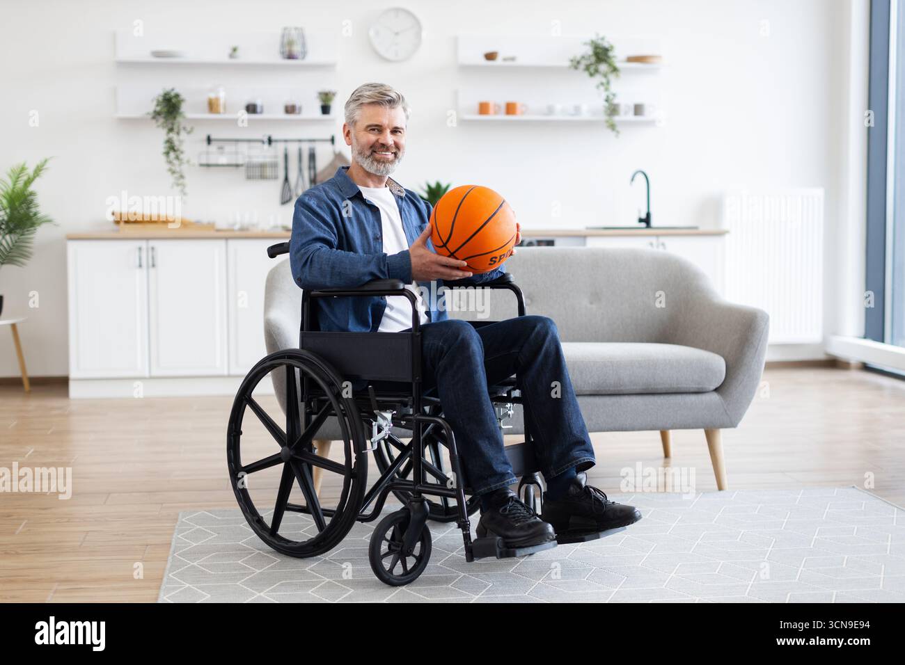 Man practicing basketball while seated in wheelchair in modern home ...