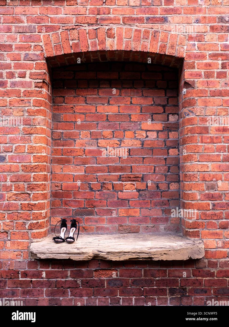Pair of black high heel shoes left on a stone ledge within an old brick ...