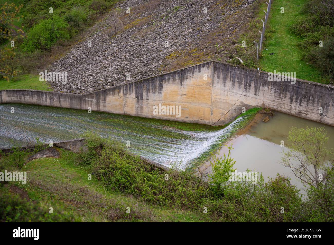 Concrete dam with water overflow in green valley. Old concrete dam with ...