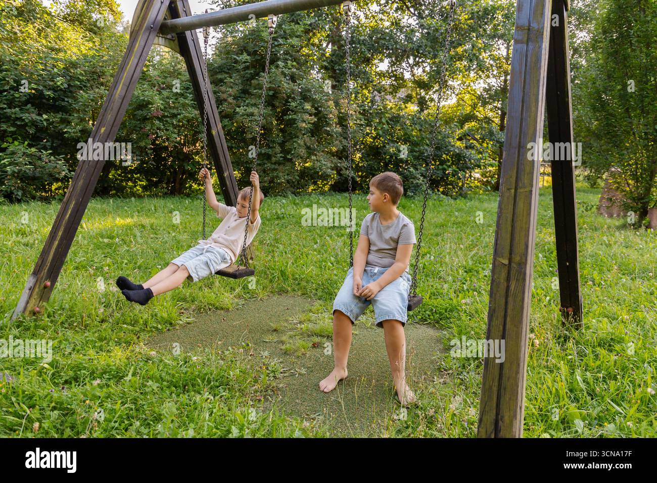Two kids are playing joyfully on a swing set in a lush green area ...