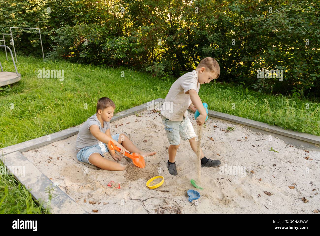 Two children are happily playing in a sandbox, digging with colorful ...