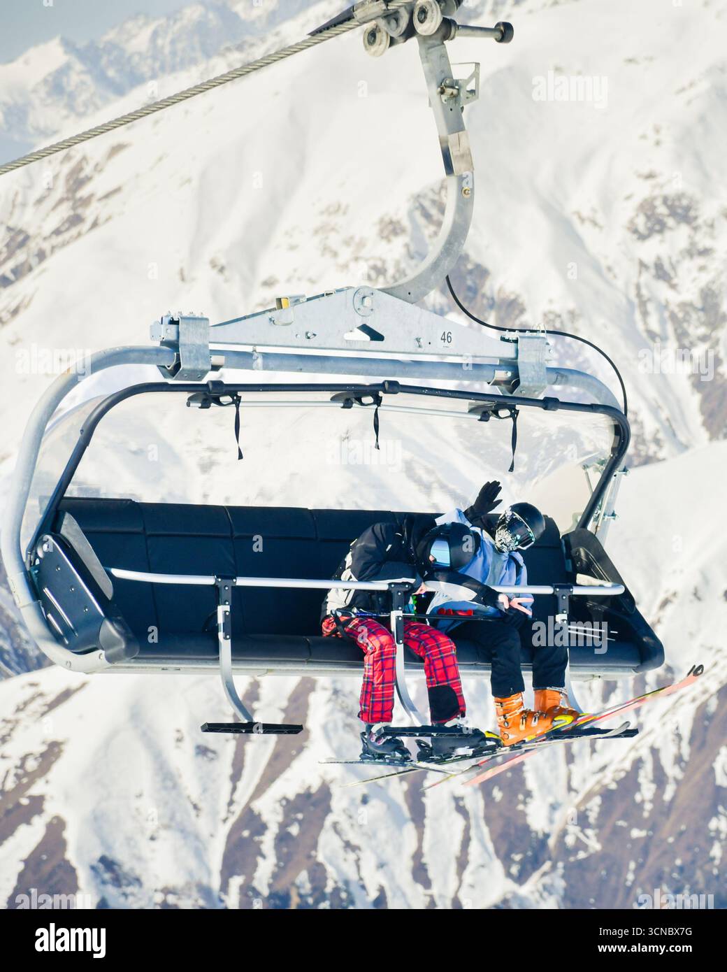 Two skiers sitting on chairlift above snowy alpine landscape, concept ...
