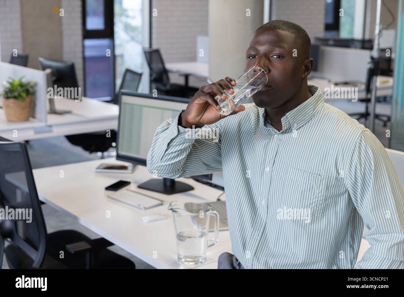 African american man pausing at corporate desk drinking water from ...