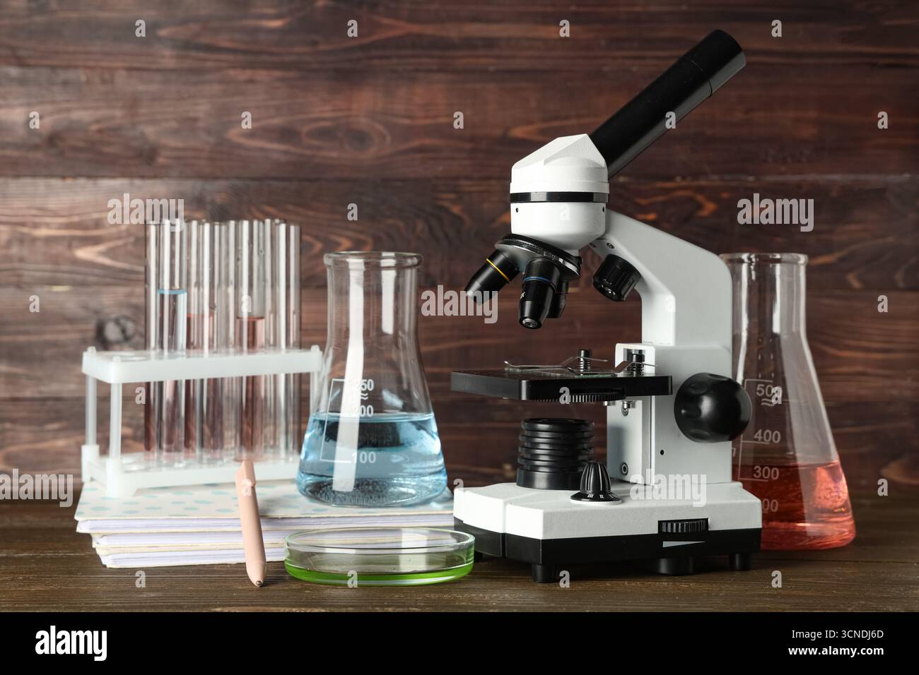 Modern microscope with chemical flasks on table against wooden ...