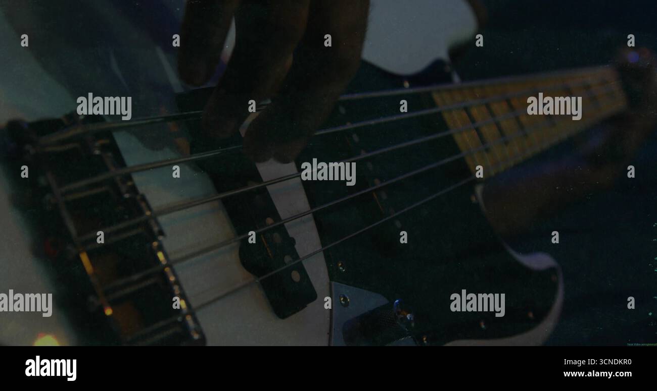 Left hand pressing and plucking strings on white bass fretboard in dim ...