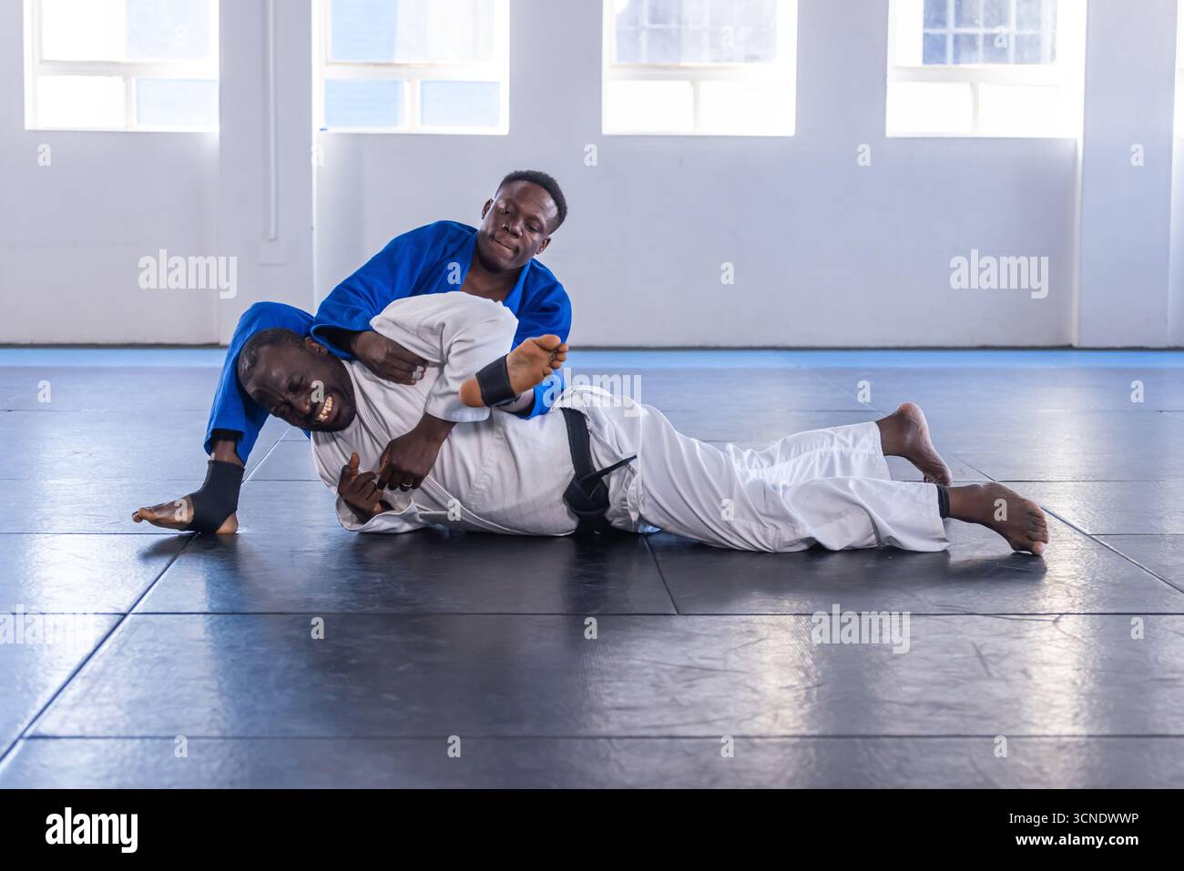 African american male training partners grappling on padded mat in dojo ...