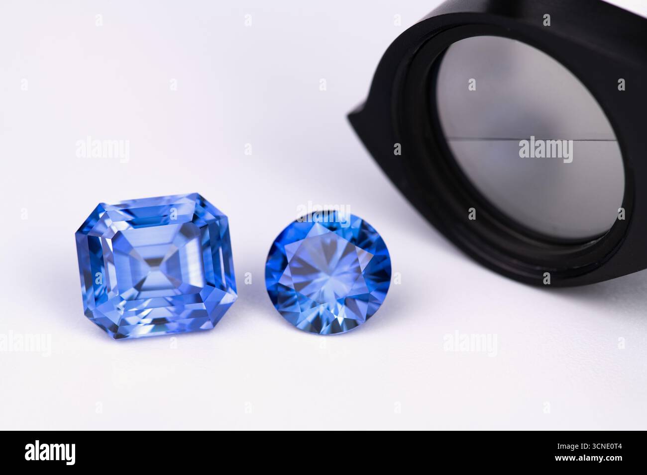 Two blue gems are on a table next to a magnifying glass. The gems are ...