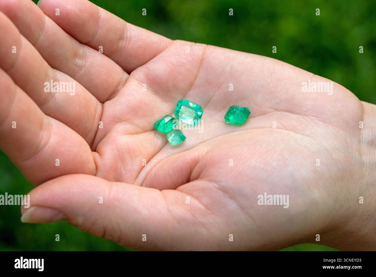 A hand holding a handful of green gemstones. The gemstones are small ...