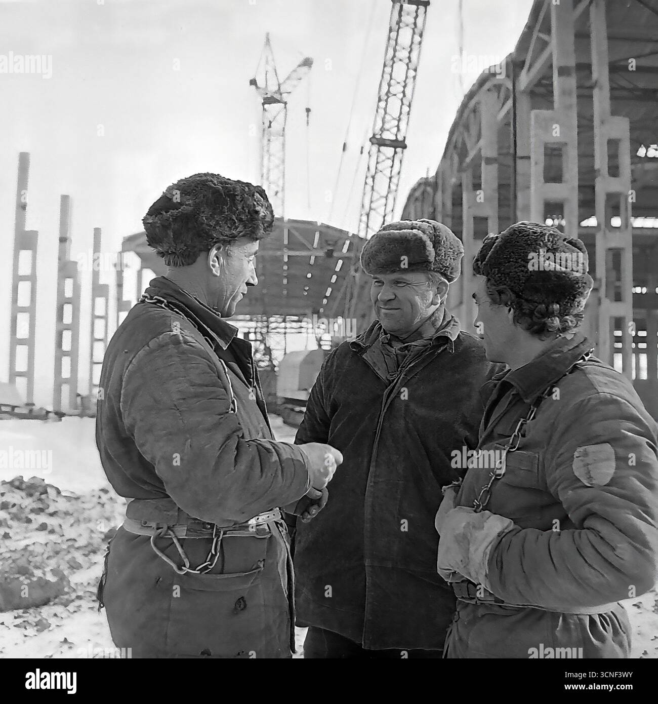 Three Soviet construction workers in winter work clothes engage in a ...