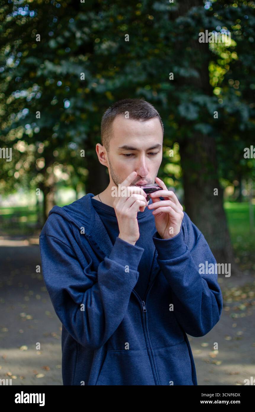 A young man is playing a harmonica while standing on a path in a green ...