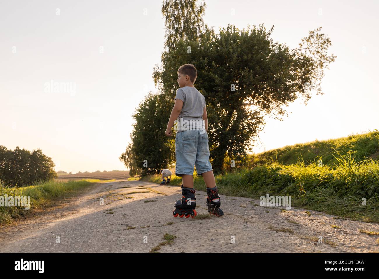 Two friends are enjoying a warm sunny day by inline skating on a quiet ...