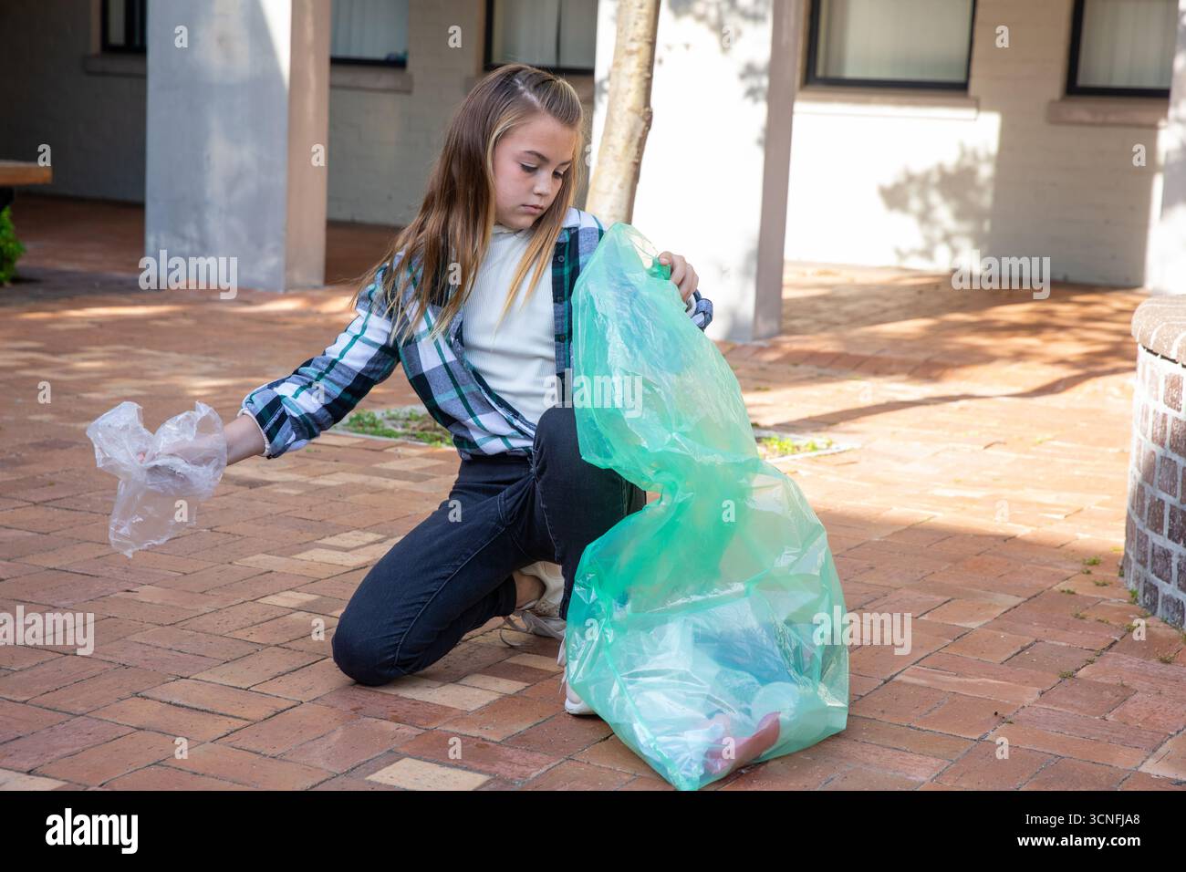 Child female picking up small plastic bag on brick courtyard with large ...