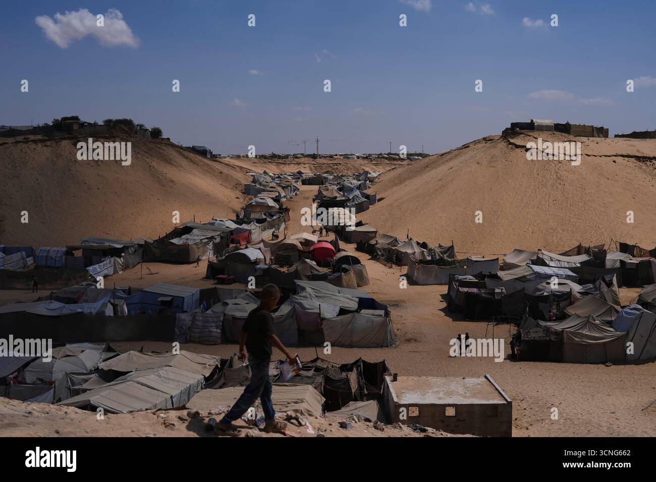 Displaced Palestinians walks through a tent camp in Muwasi, an area ...