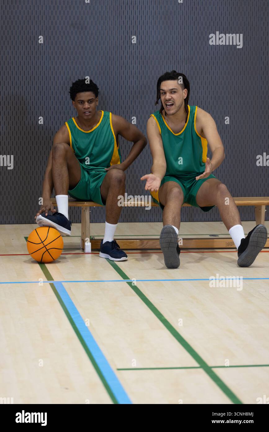 Two male basketball players wearing green jerseys sitting on bench at ...