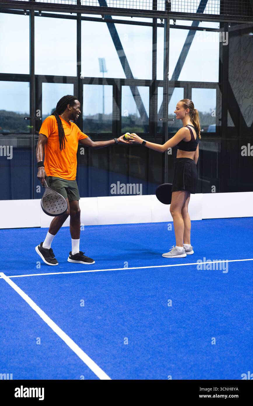 Diverse friends holding padel rackets and passing yellow ball on blue ...