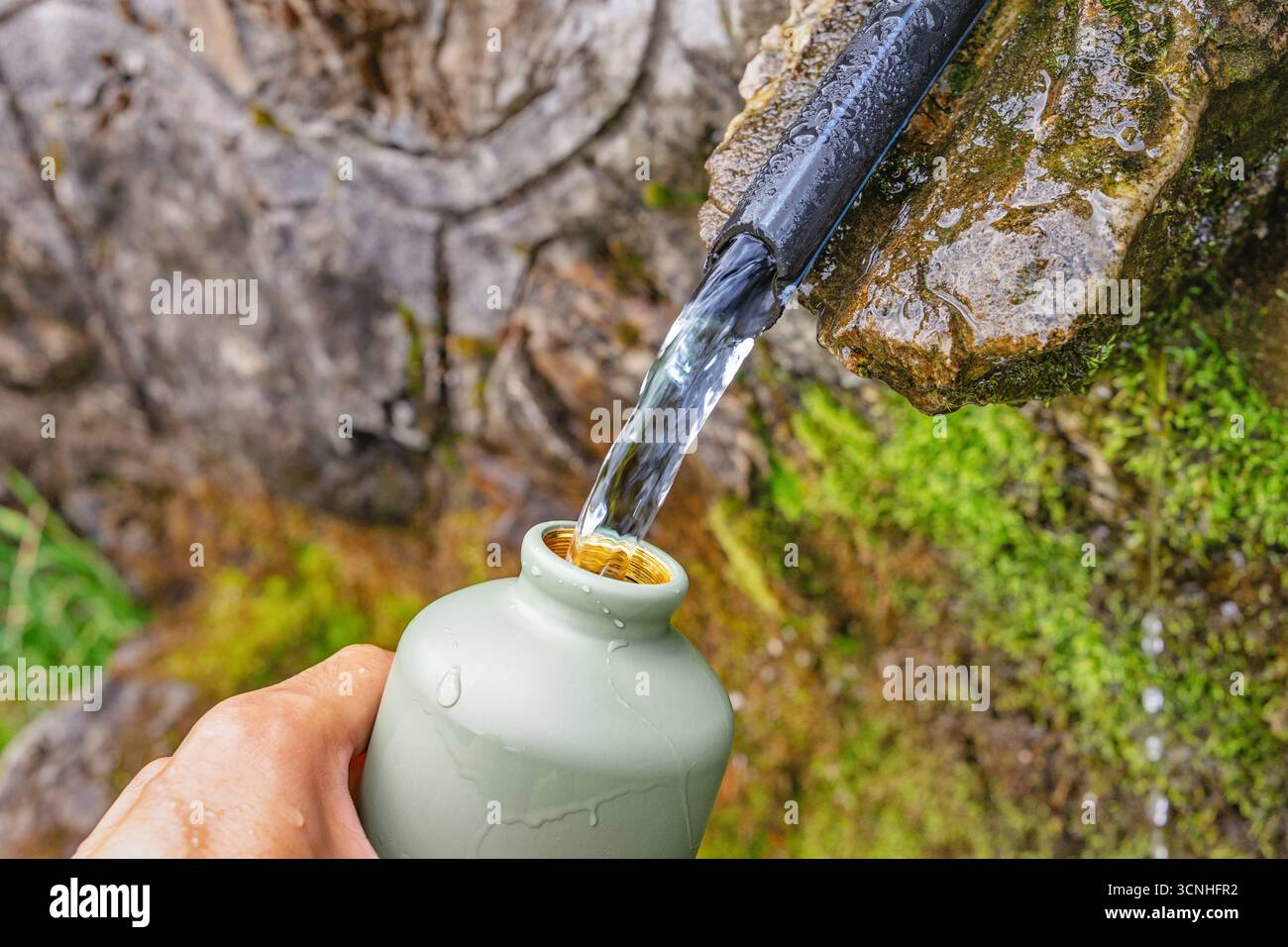 Hand refilling a reusable water bottle with natural spring water from a ...