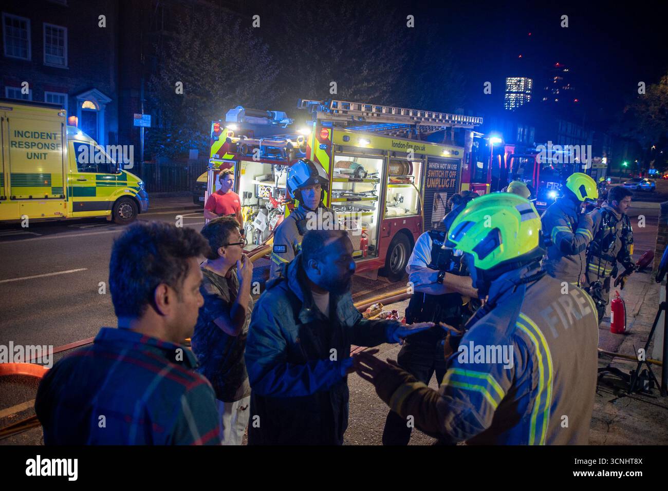 The hotel receptionist and the guests talk with a fire fighter outside ...