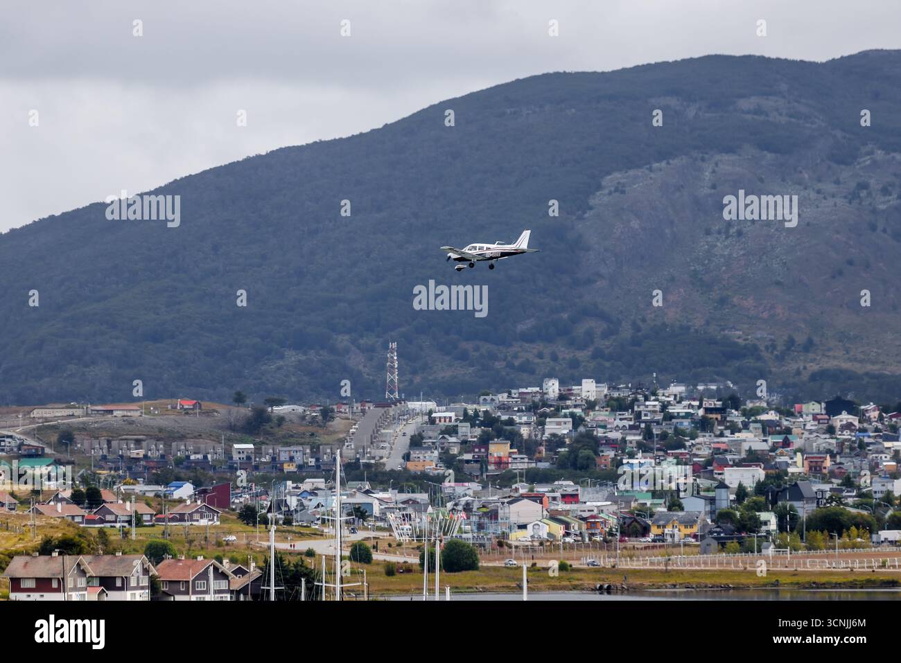 A small fixed-wing aircraft flies above the tree-covered hills of ...