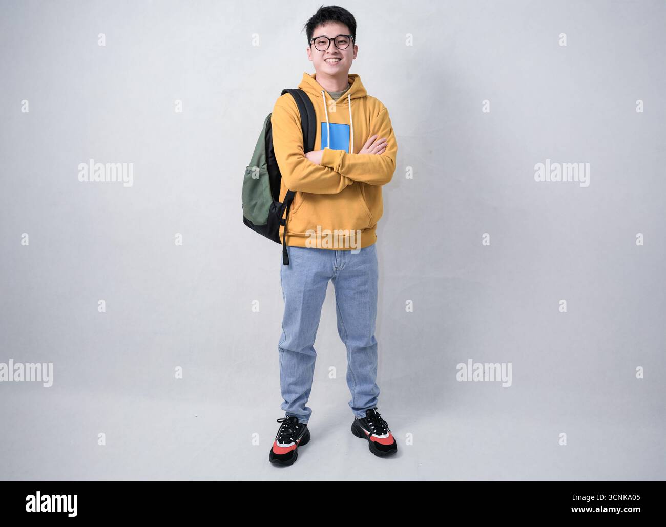 A stylish young man in a mustard hoodie and backpack poses in a clean ...