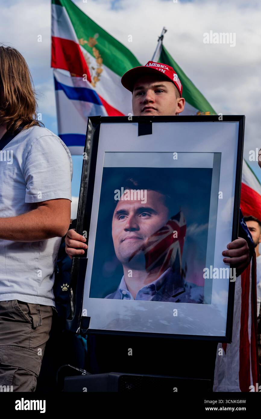 A mourner wearing a MAGA baseball cap holds aloft a framed photo of the ...