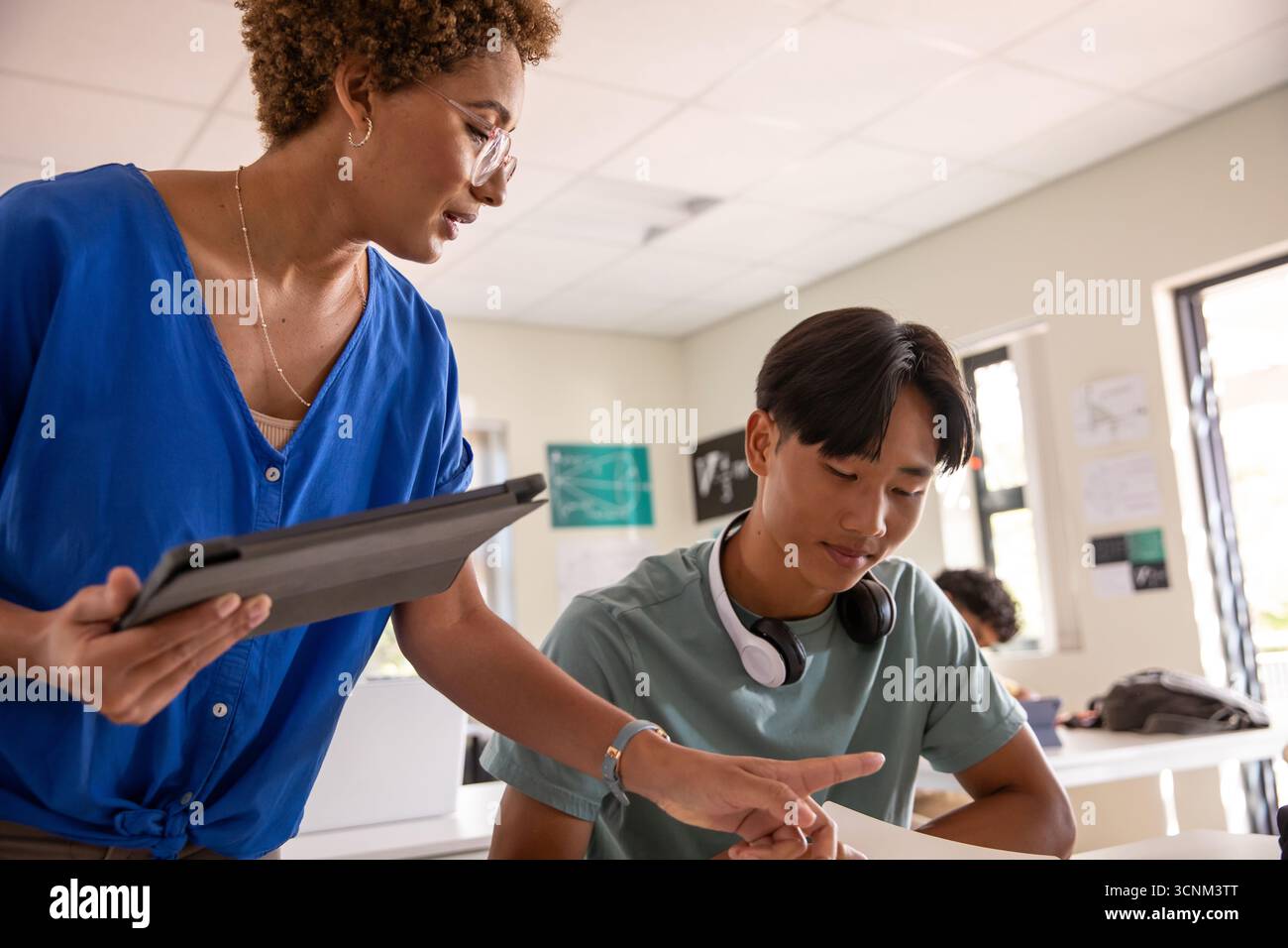 Female teacher and asian teen student wearing headphones holding tablet ...